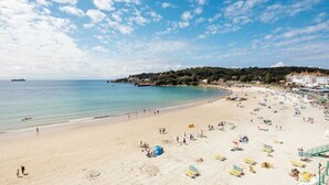 Uma extensa praia de areia com mar calmo, algumas pessoas e um navio ao longe.