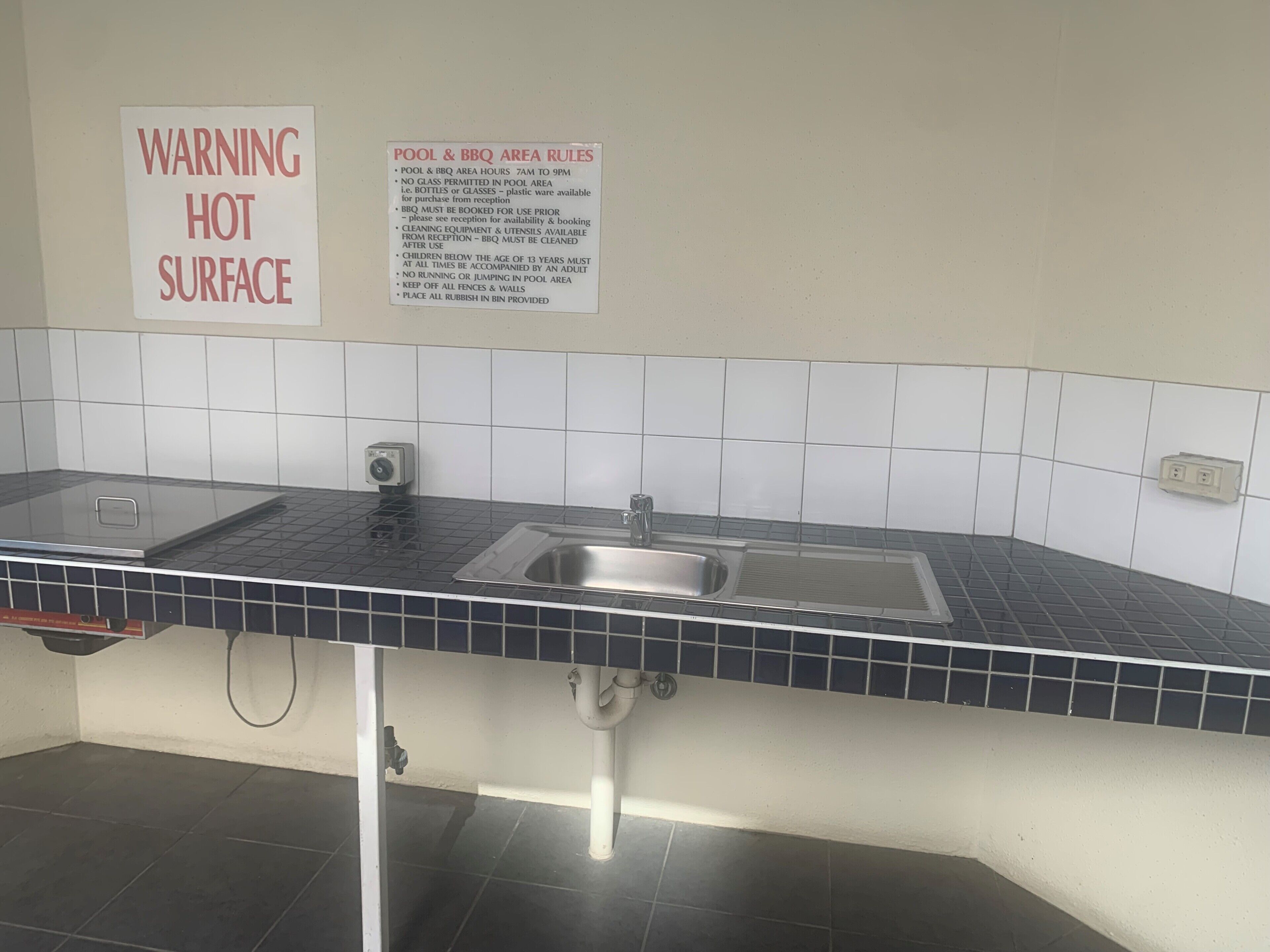 Uma cozinha com pia, um aviso sobre superfície quente e regras para a piscina e churrasqueira.