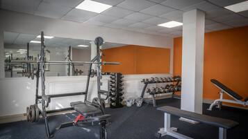 Uma academia com equipamentos de musculação, bancos e um espelho grande na parede.