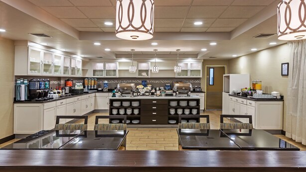 Espaço de refeições de hotel com buffet central, diversos arranjos de assento e luminárias pendentes.