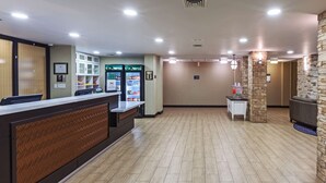 Área de recepção de hotel com balcão, geladeira abastecida com bebidas, placa na parede e um pilar de pedra.