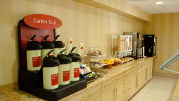 Disposição de buffet com recipientes identificados, uma máquina de café e uma saladeira de frutas.