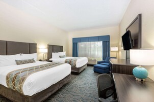 Quarto de hotel com duas camas, uma escrivaninha, uma cadeira, uma televisão e uma janela com cortinas.