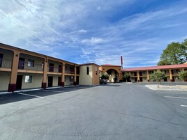 Um motel com vários andares, pátio central, estacionamento externo e céu claro.