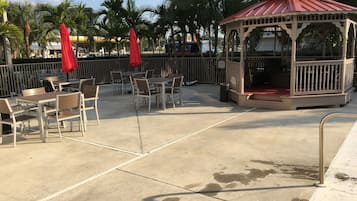 Área externa com mesas, cadeiras, um gazebo e palmeiras.