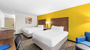 Quarto de hotel com duas camas, uma escrivaninha, uma cadeira e uma mesinha.