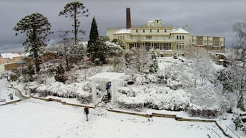 Um edifício grande com uma chaminé notável, rodeado por árvores cobertas de neve e um coreto.