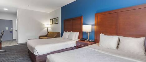 Quarto de hotel com duas camas, uma mesa com abajur, uma cadeira e uma porta.