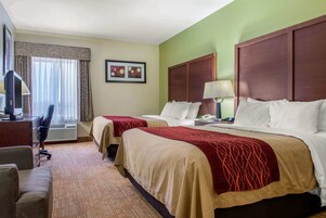 Quarto de hotel com duas camas, uma escrivaninha com cadeira, televisão e janela com cortinas.