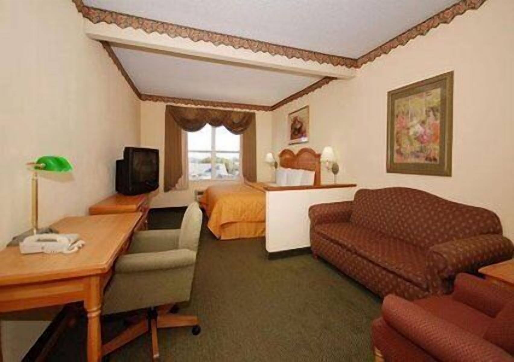 Quarto de hotel com cama, escrivaninha com telefone, televisão, sofá e um quadro na parede.