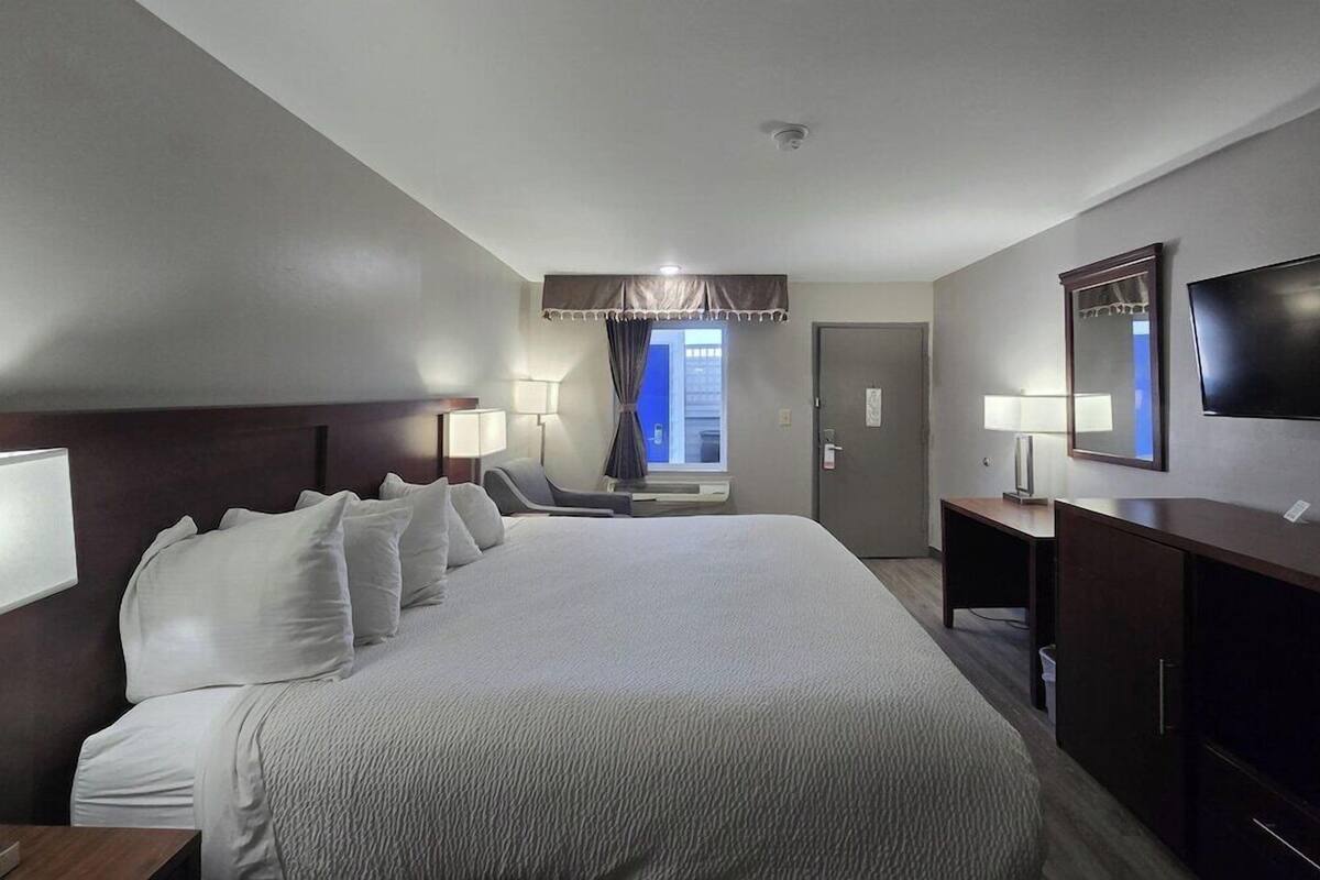 Quarto de hotel com cama grande, mesas de cabeceira, escrivaninha, televisão e janela com cortinas.