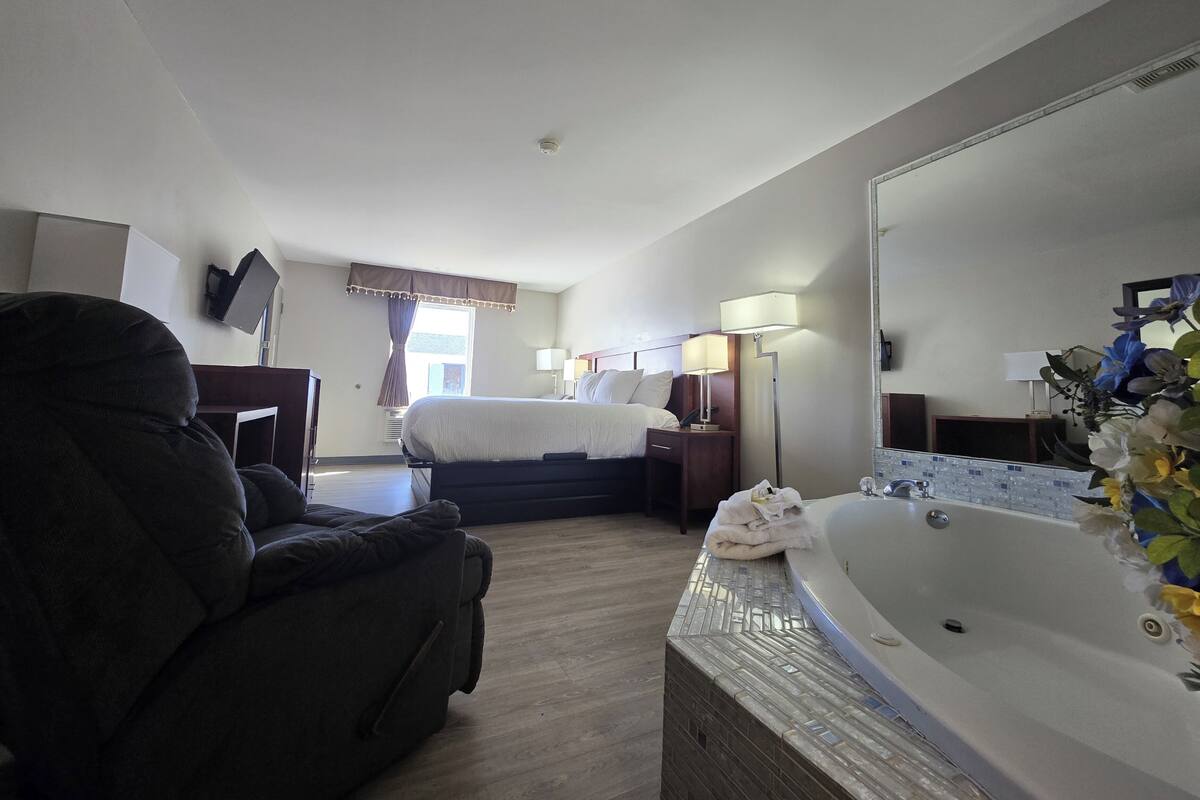 Quarto de hotel com cama, um espelho grande, banheira e escrivaninha com cadeira.