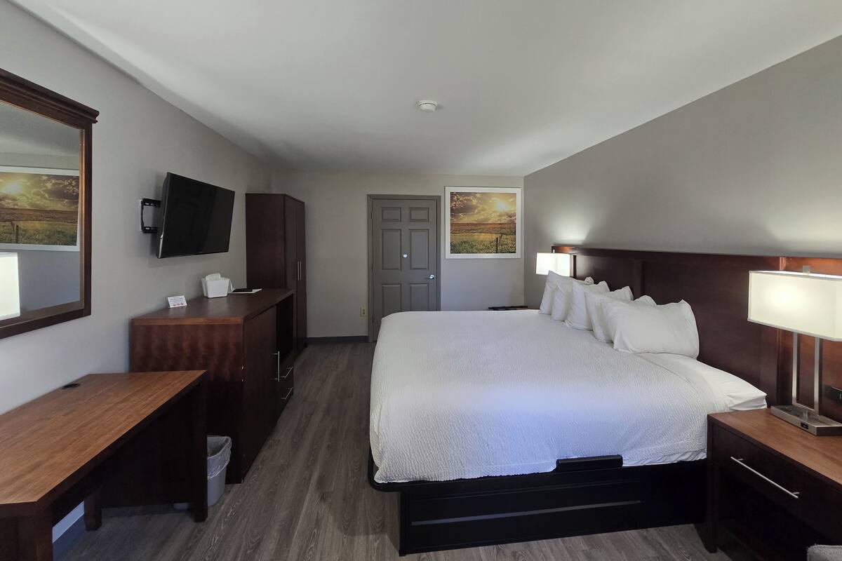 Quarto de hotel com cama, mesas de cabeceira, televisão, escrivaninha e porta.