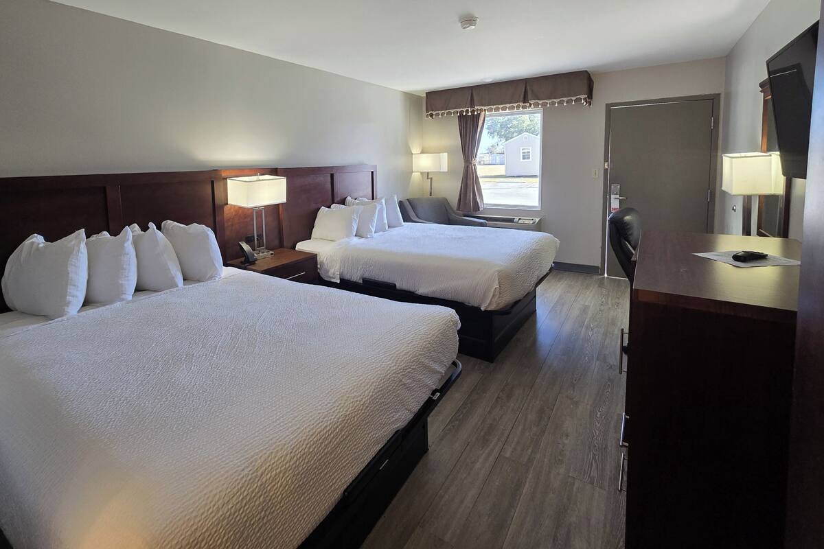Quarto de hotel com duas camas, uma escrivaninha, uma cadeira, uma televisão e uma janela com cortinas.
