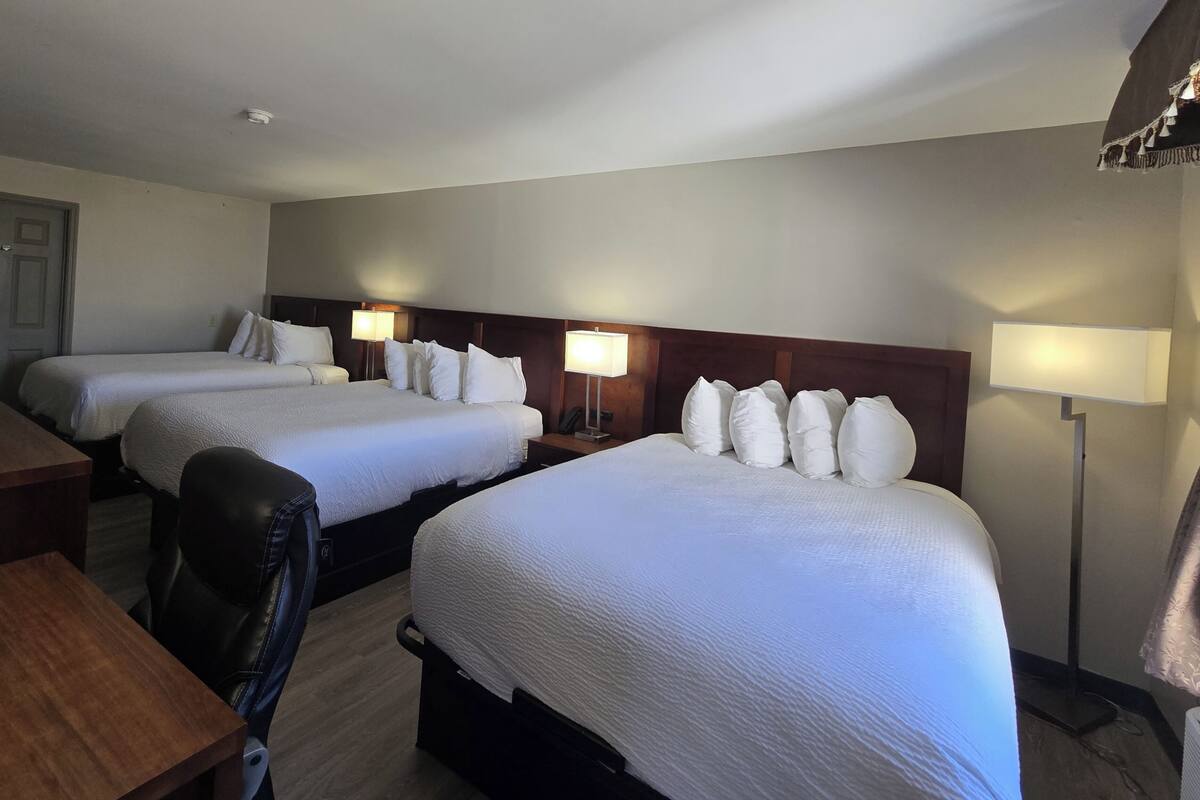 Quarto de hotel com duas camas, uma escrivaninha e uma cadeira.