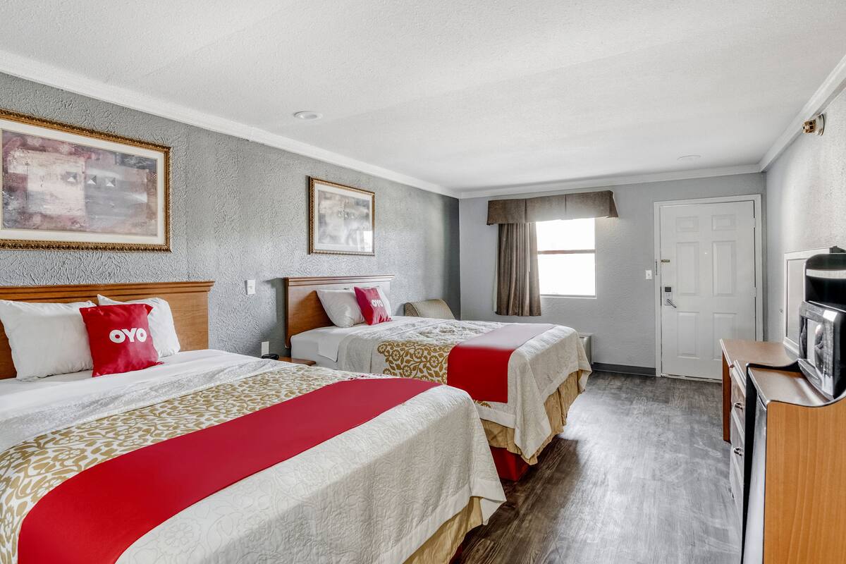 Quarto de hotel com duas camas, televisão e uma porta.
