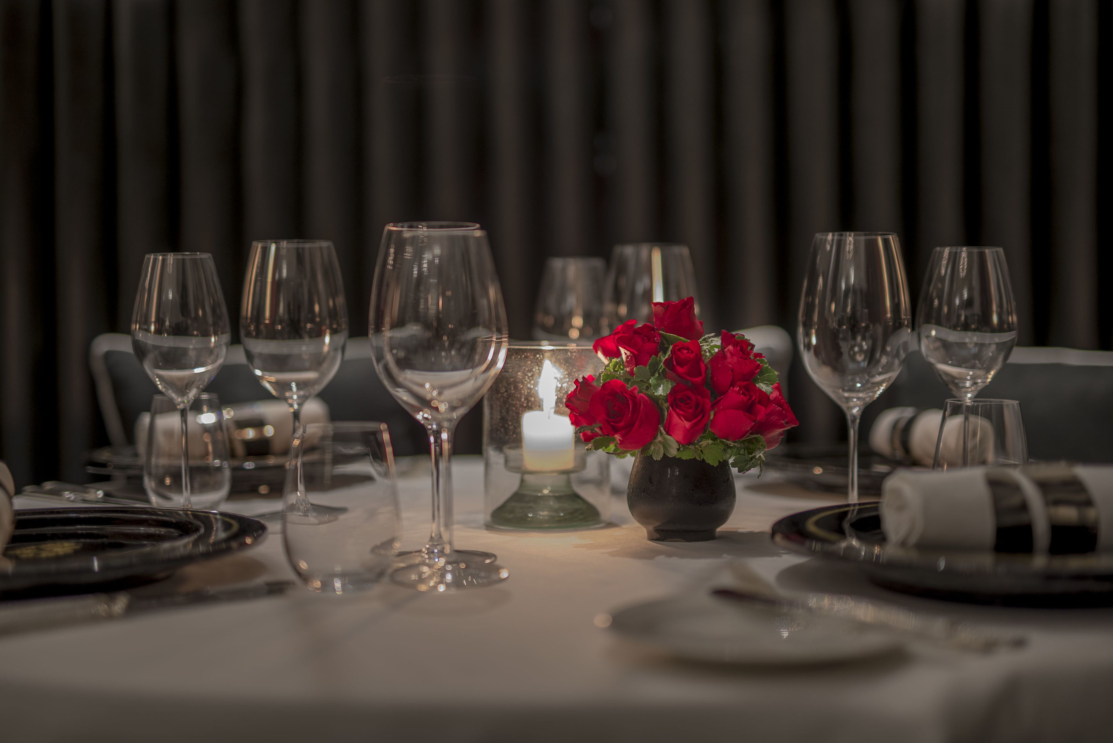 Uma mesa posta para refeição, com vários copos de vinho e um castiçal como centro.