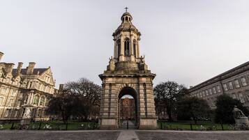 Um edifício histórico com uma entrada imponente, ladeado por árvores e um calçadão.