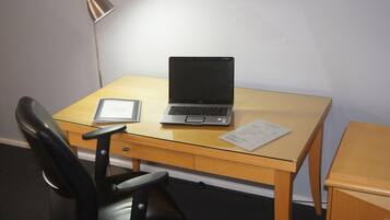 Um pequeno escritório com escrivaninha de madeira, um laptop, uma cadeira e uma luminária.