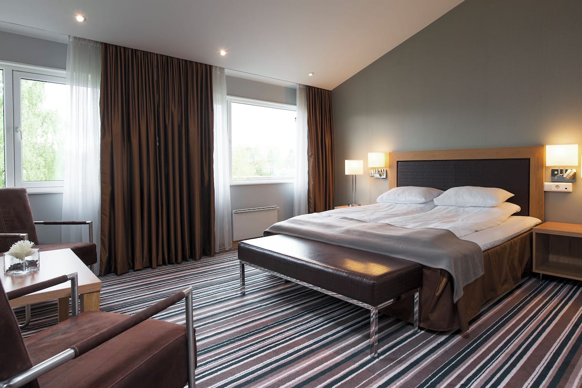 Quarto de hotel com cama grande, duas luminárias de cabeceira, escrivaninha com cadeira e vista para o exterior pela janela.