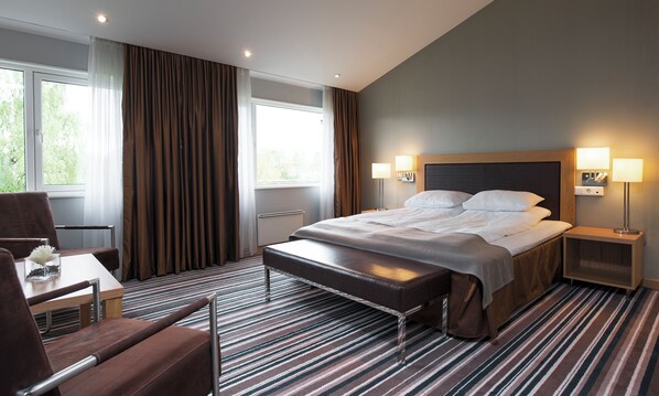Quarto de hotel com cama grande, duas luminárias de cabeceira, escrivaninha com cadeira e vista para o exterior pela janela.