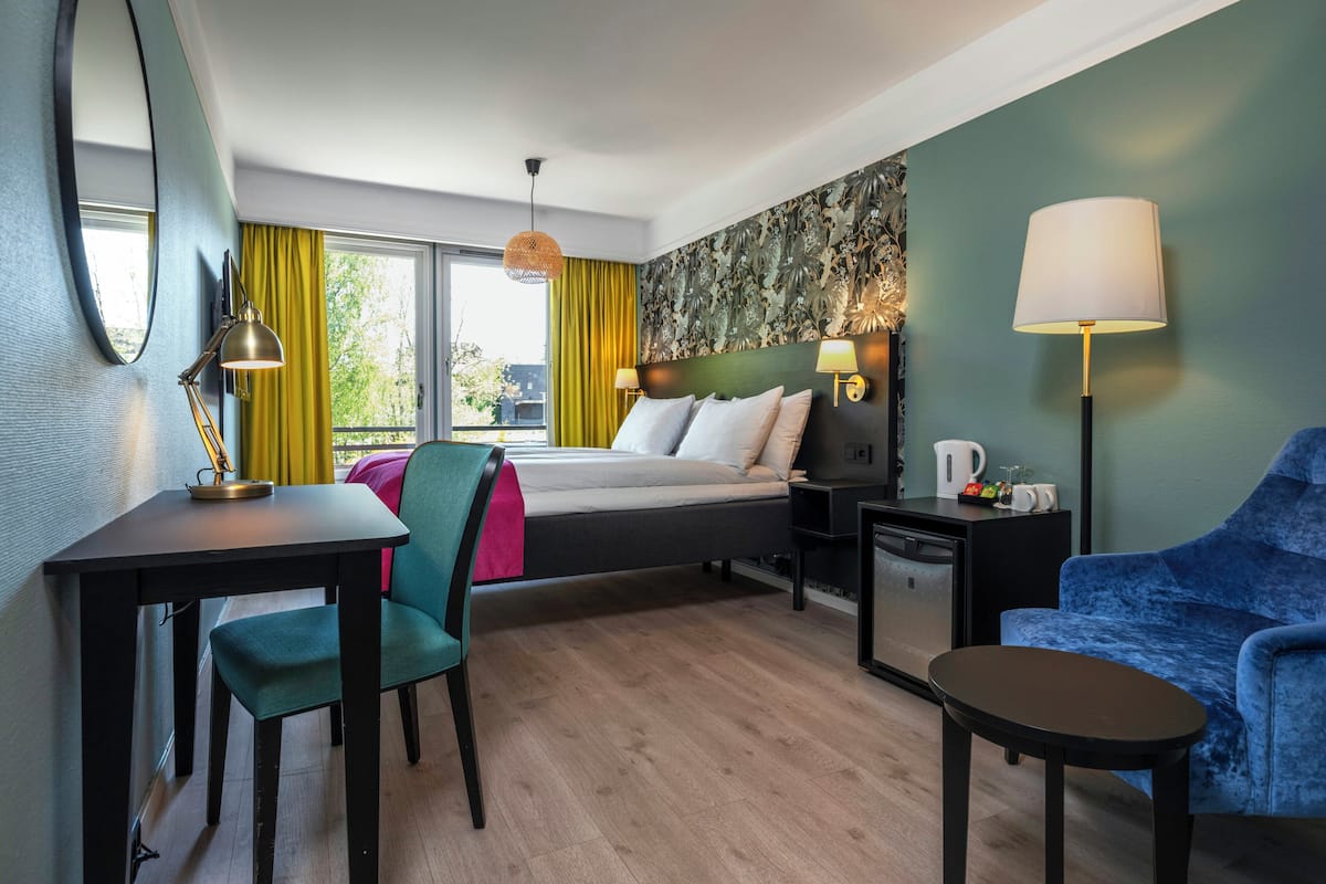 Quarto de hotel com cama, escrivaninha, cadeira e uma pequena mesa.