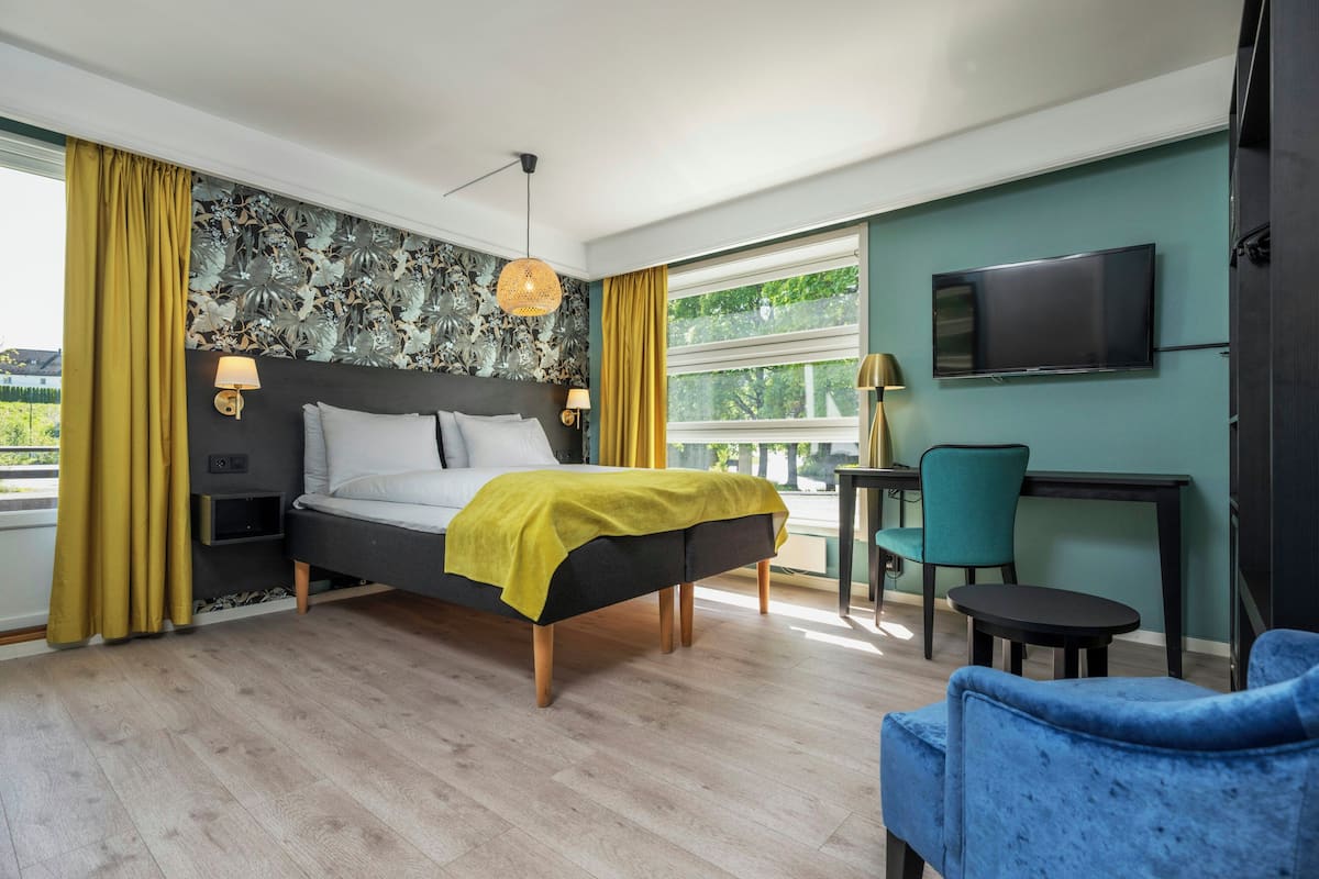 Quarto de hotel moderno com cama, escrivaninha, cadeira e televisão.