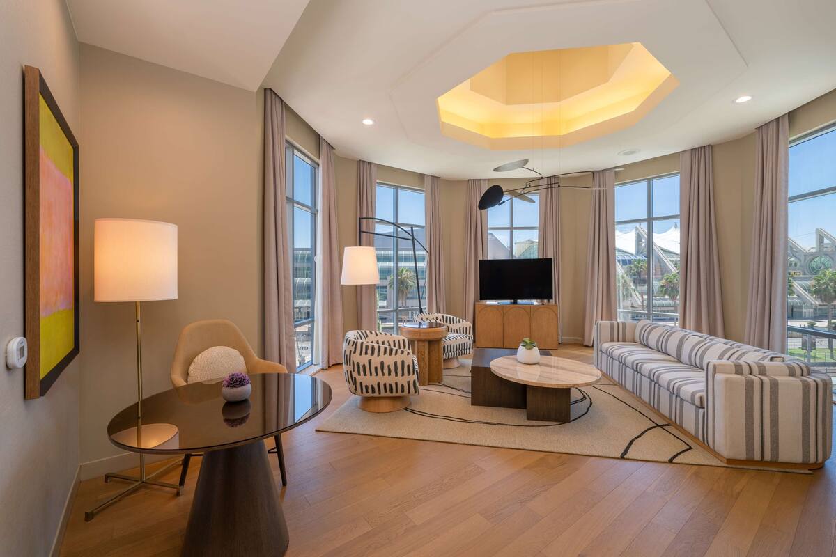 Quarto de hotel moderno com um sofá grande, uma mesa de jantar e uma televisão.