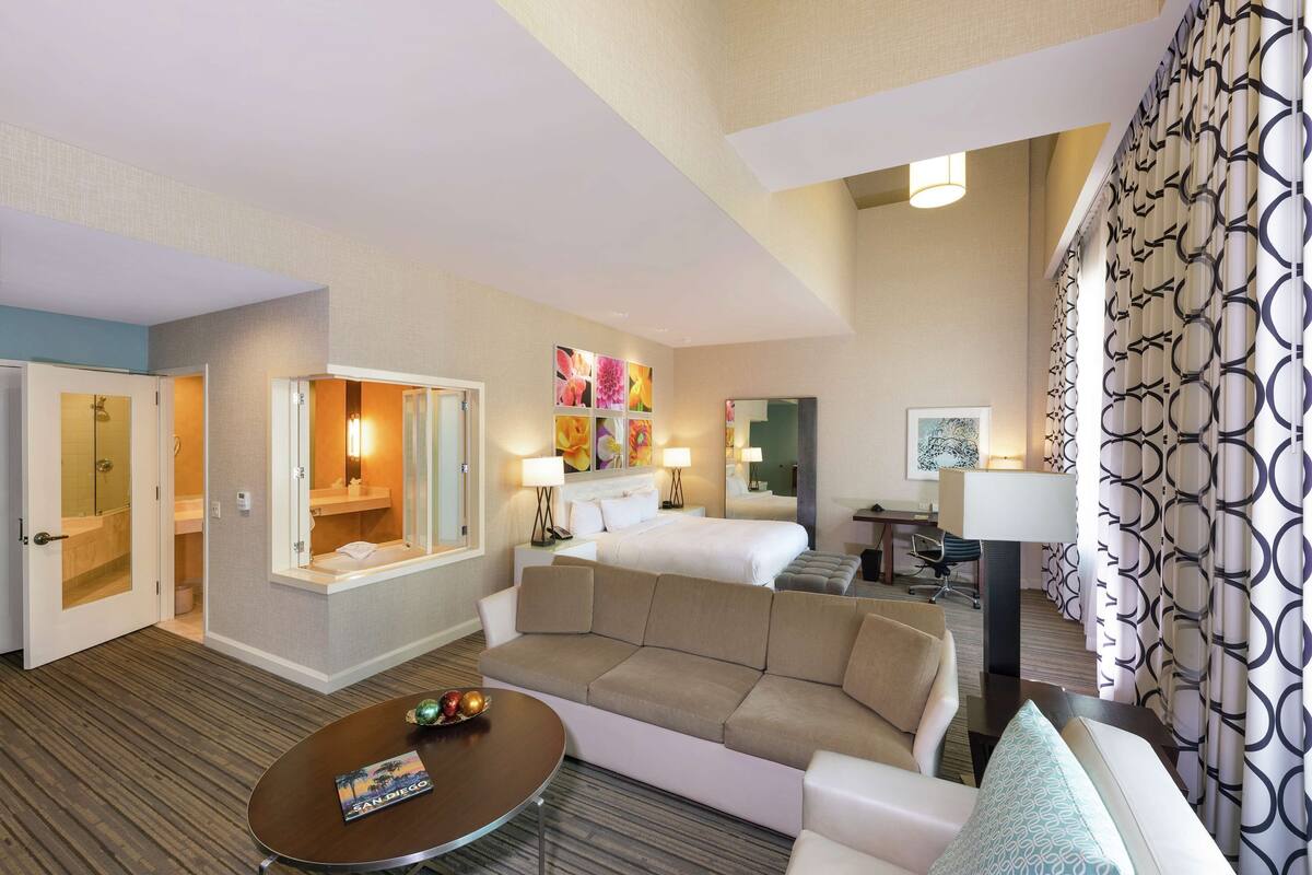 Quarto de hotel com cama, sofá, escrivaninha, espelho e banheiro.