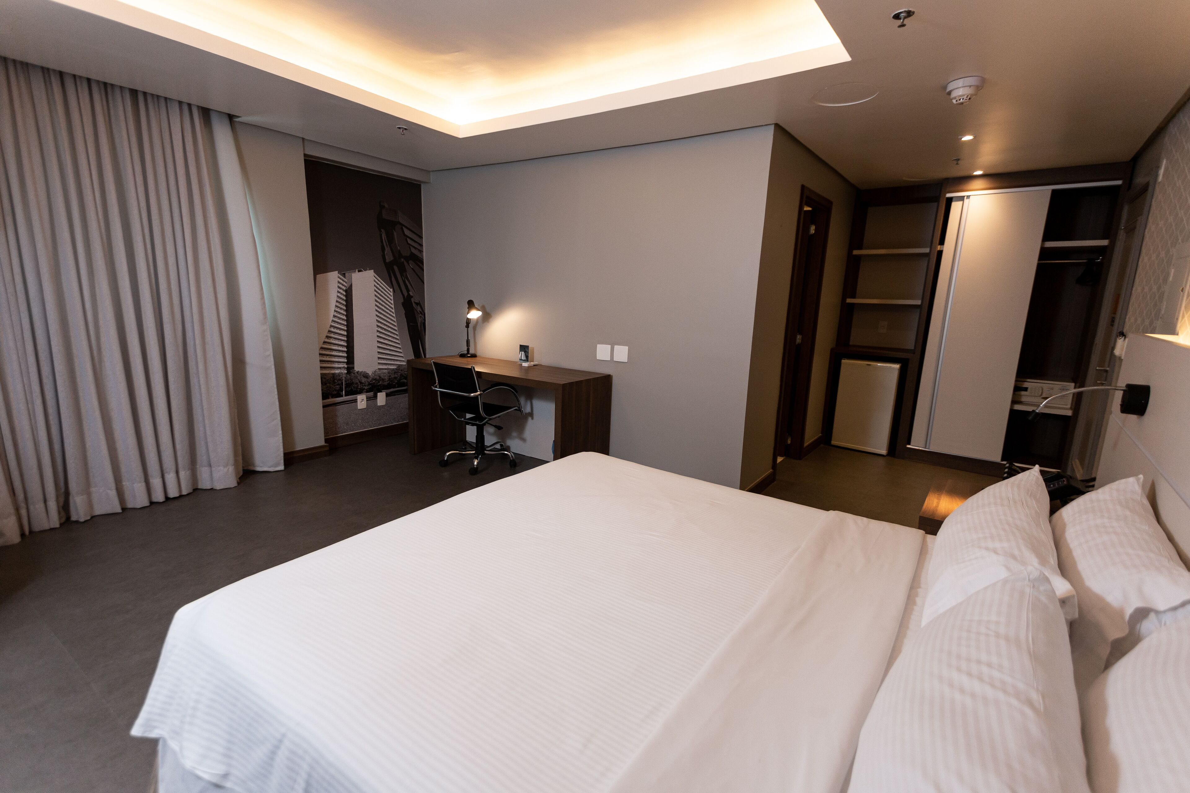 Quarto de hotel moderno com uma cama grande, uma escrivaninha com cadeira, um guarda-roupa e uma casa de banho.