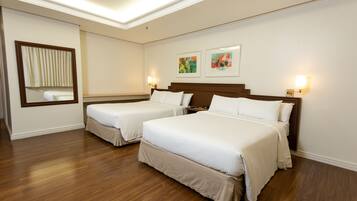 Quarto de hotel com duas camas, piso de madeira, um espelho grande e duas luminárias fixadas na parede.