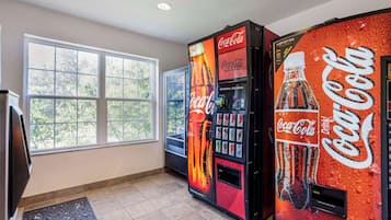 Quarto com duas máquinas de venda automática de Coca-Cola e uma janela com vista para vegetação.
