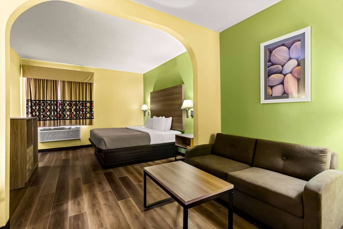 Quarto de hotel com uma cama, um sofá, uma mesinha, um quadro na parede e uma janela com cortinas.