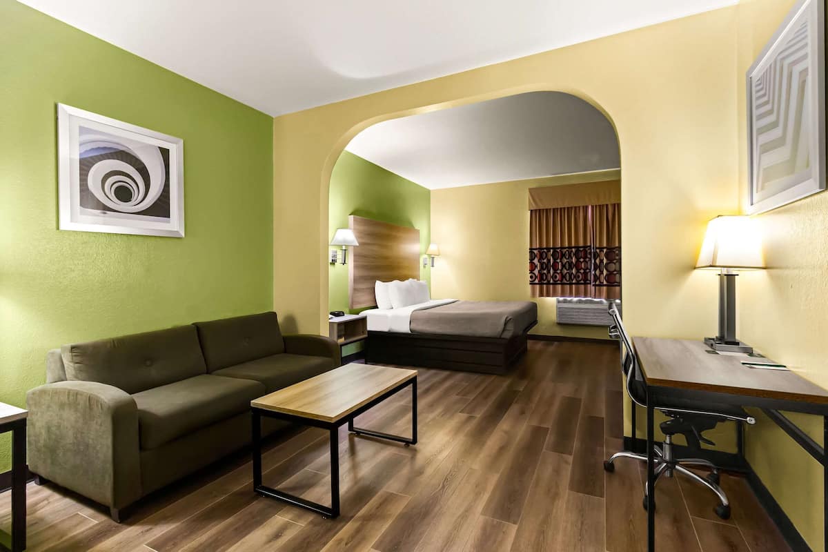 Quarto de hotel com sofá, mesa pequena, escrivaninha, cama e quadro na parede.