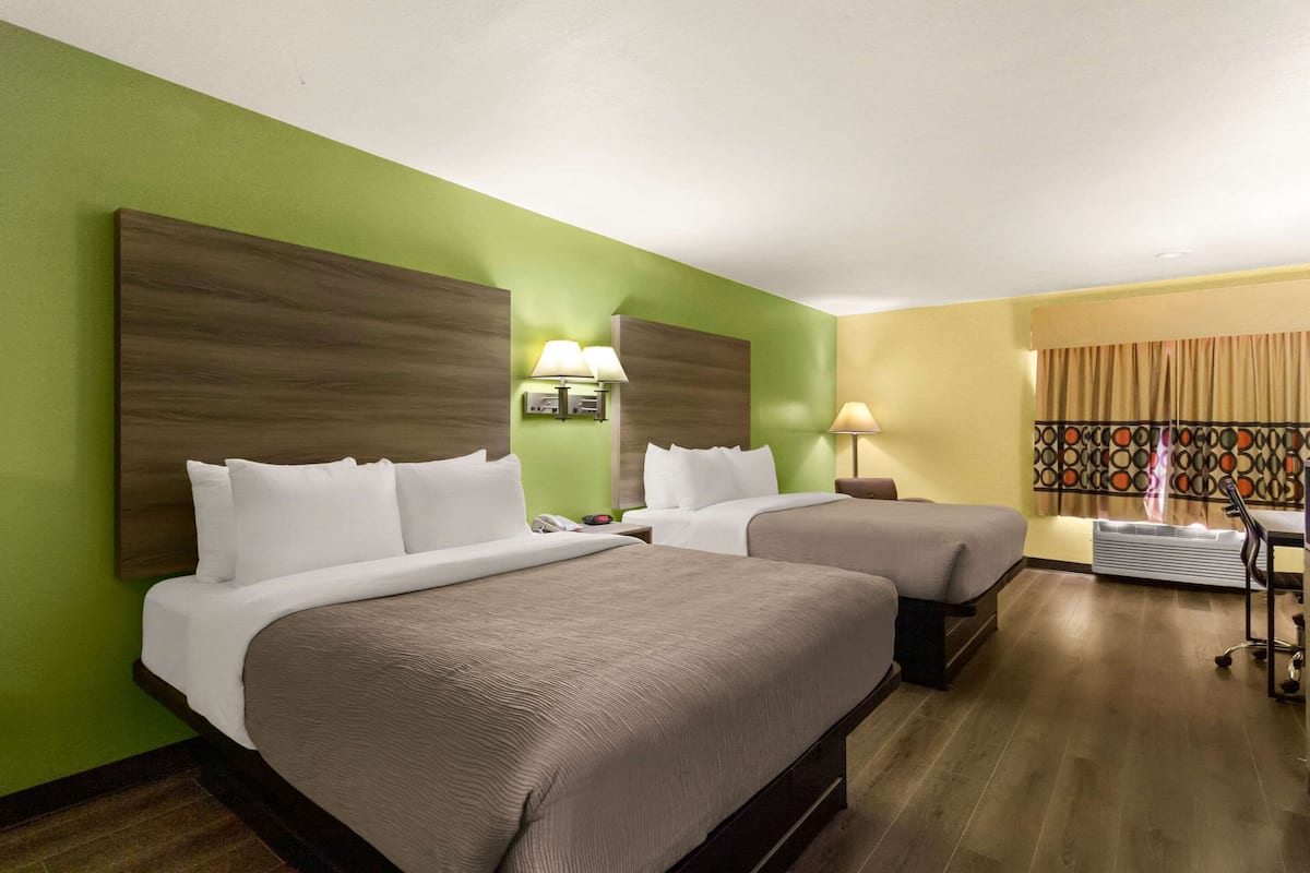 Quarto de hotel com duas camas, paredes verdes e chão de madeira.