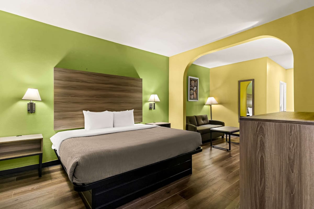 Quarto de hotel com uma cama grande, duas mesas de cabeceira, uma cadeira, uma escrivaninha e um espelho.