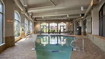 Piscina interior com sinalização clara, piso revestido e grandes janelas que permitem entrada de luz natural.