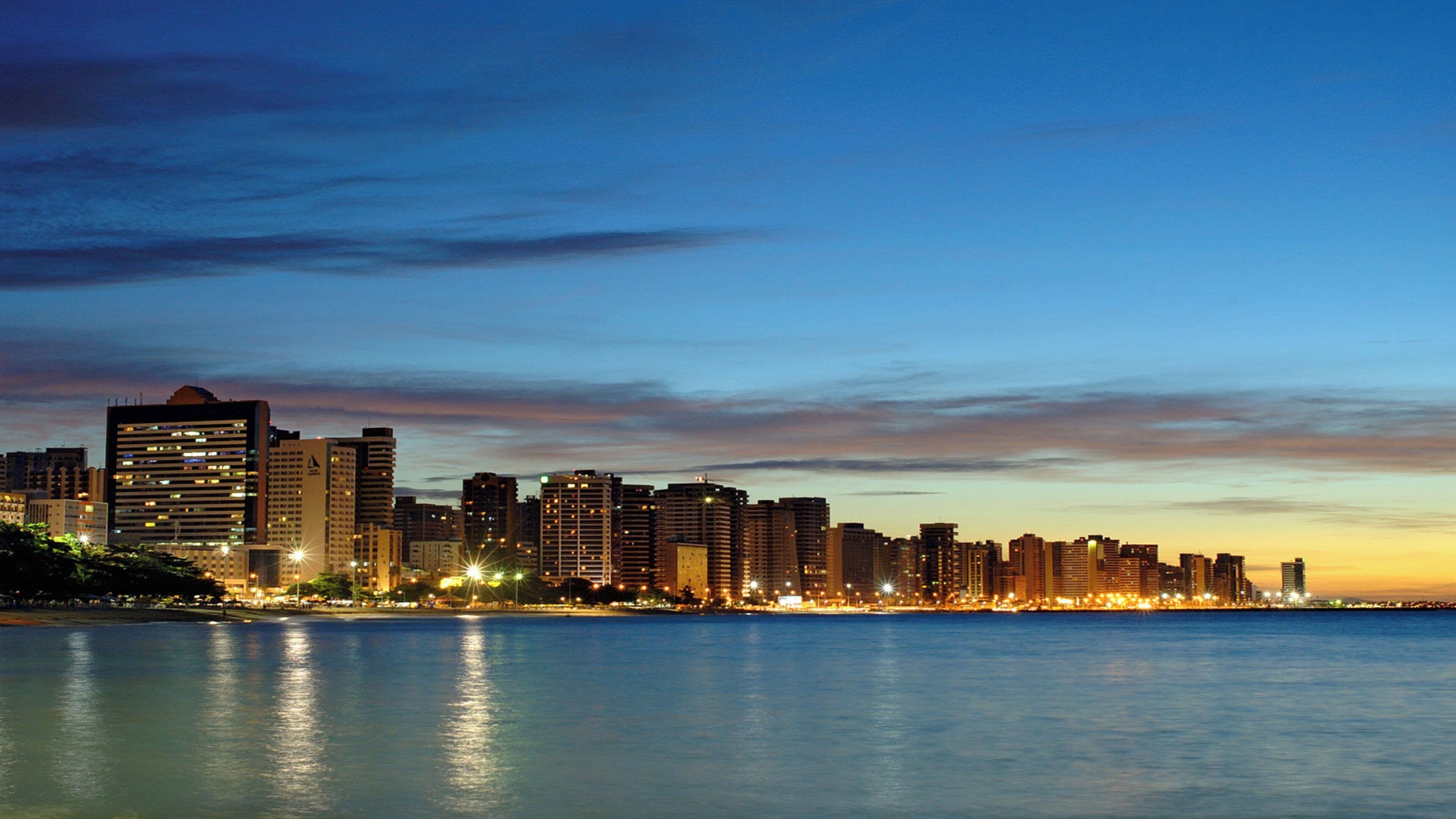 Silhueta urbana ao entardecer, com edifícios altos à beira-mar.