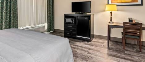 Quarto de hotel com cama, escrivaninha com lâmpada, televisão e micro-ondas.