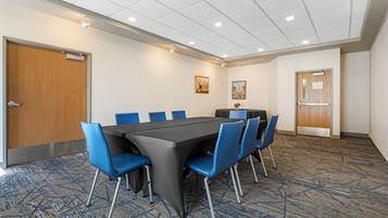 Uma sala de conferências com uma mesa retangular, cadeiras azuis e piso carpeteado.