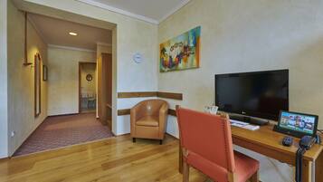 Quarto de hotel com secretária de madeira, televisão, cadeira vermelha e um quadro na parede.