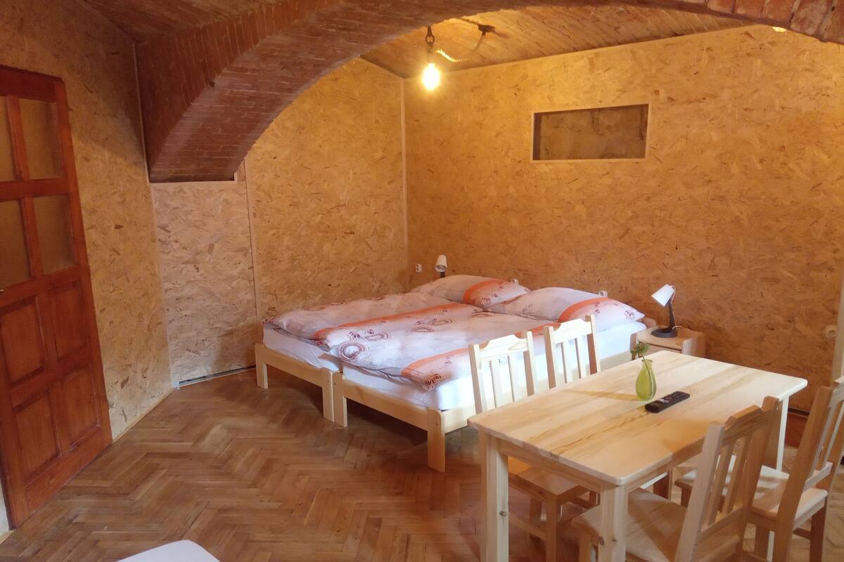 Um quarto acolhedor com uma cama de madeira, uma mesinha com cadeiras e um chão com padrão losango.