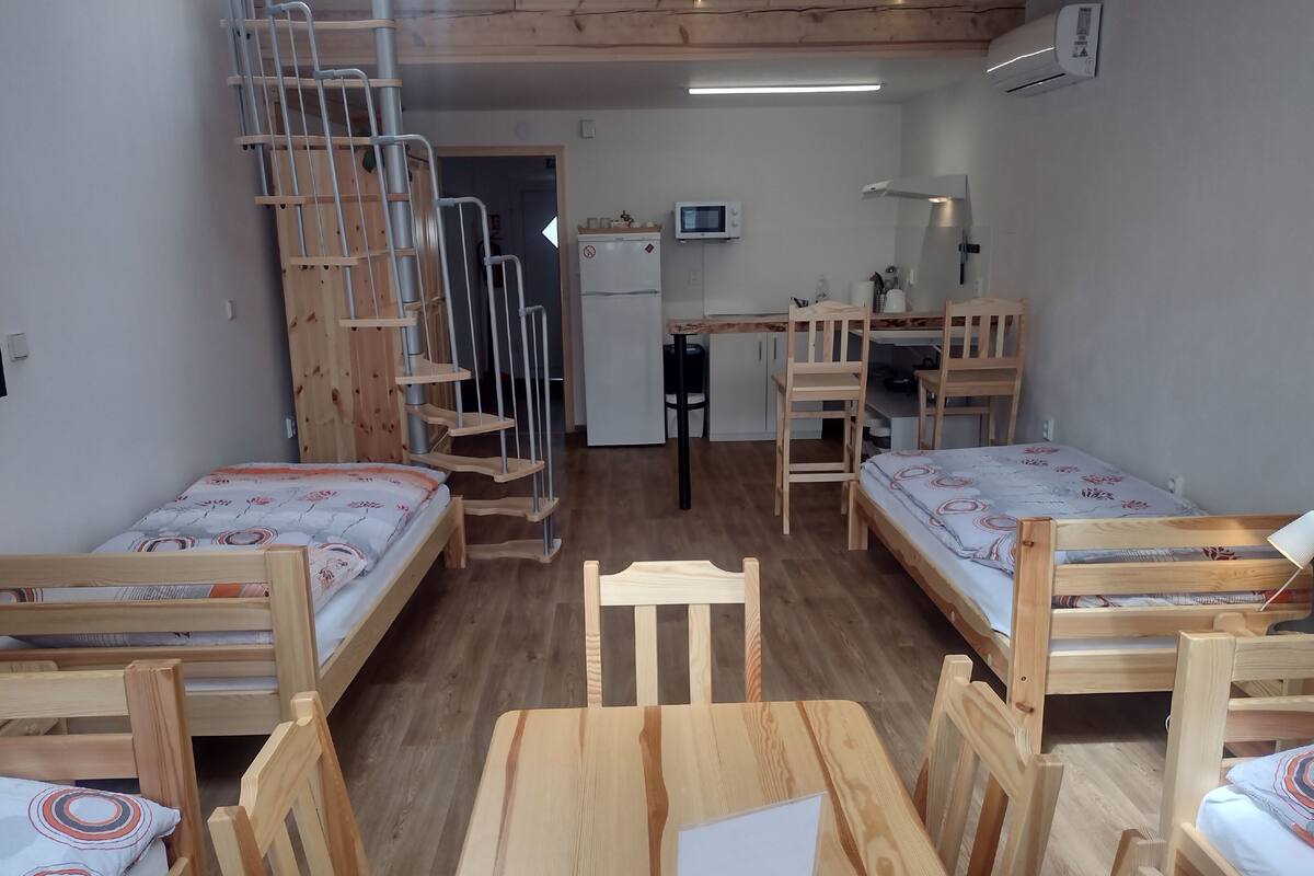 Quarto pequeno com duas camas de madeira, uma escrivaninha, uma cadeira e uma mesa de madeira.