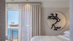 Quarto com cama, vista para o mar, uma peça de arte circular na parede e varanda com mesa e cadeiras.