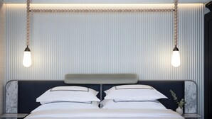 Cama bem arrumada com lençóis brancos, cabeceira escura e duas luminárias de cabeceira.
