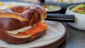 Uma mesa com um sanduíche de bagel, uma salada e uma bebida para o café da manhã.