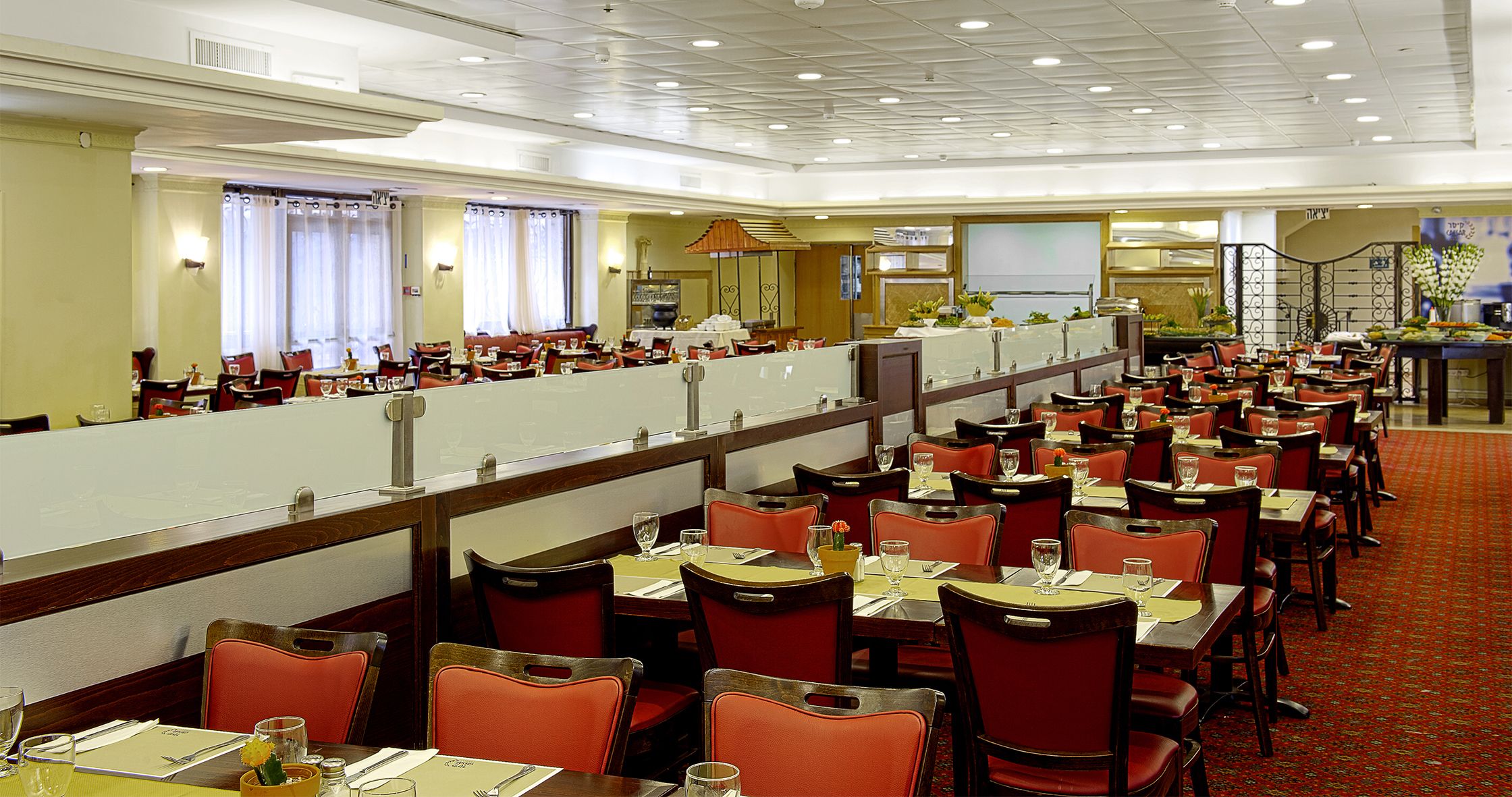 Um espaço de refeições de hotel com várias mesas e cadeiras, áreas de estar separadas e vista para a rua.