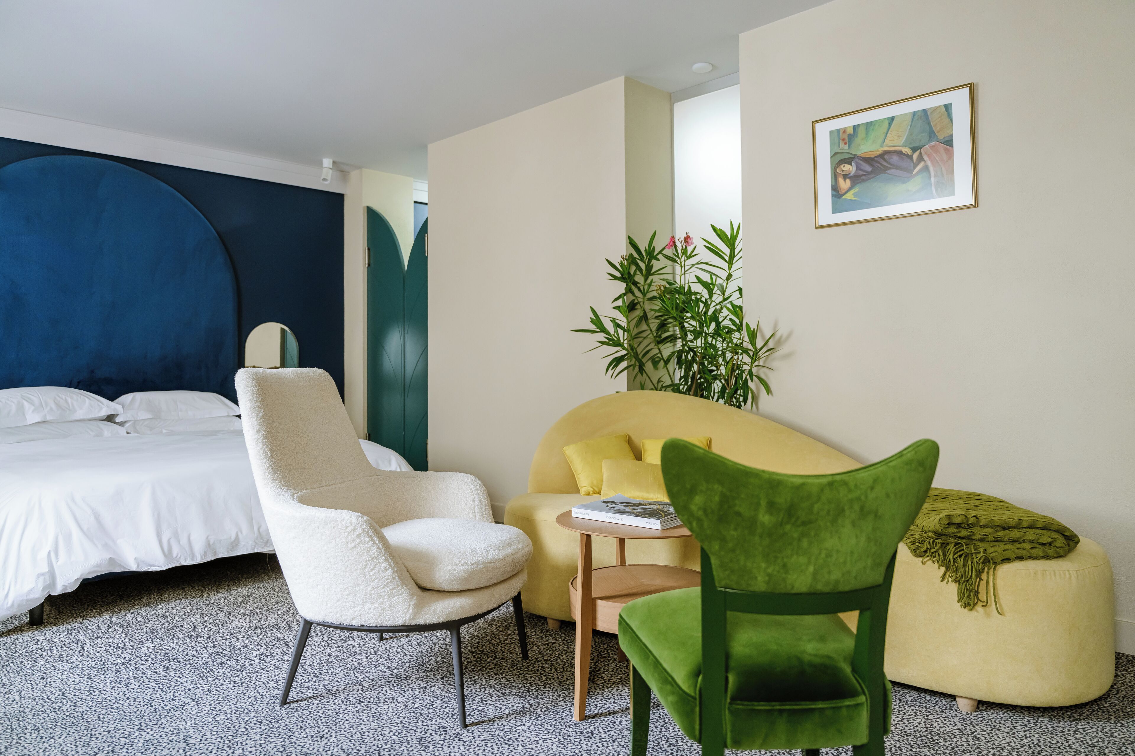 Quarto de hotel moderno com uma cama, uma poltrona branca, uma poltrona verde, um sofá amarelo e uma pequena mesa.