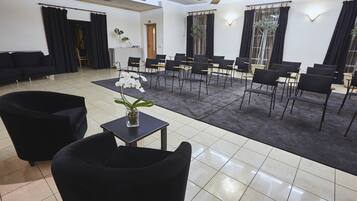 Um saguão de hotel com área de estar, balcão de recepção e uma grande janela com cortinas.