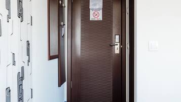 Corredor de hotel com carpete azul, porta de madeira com placa de segurança e parede com detalhes decorativos.